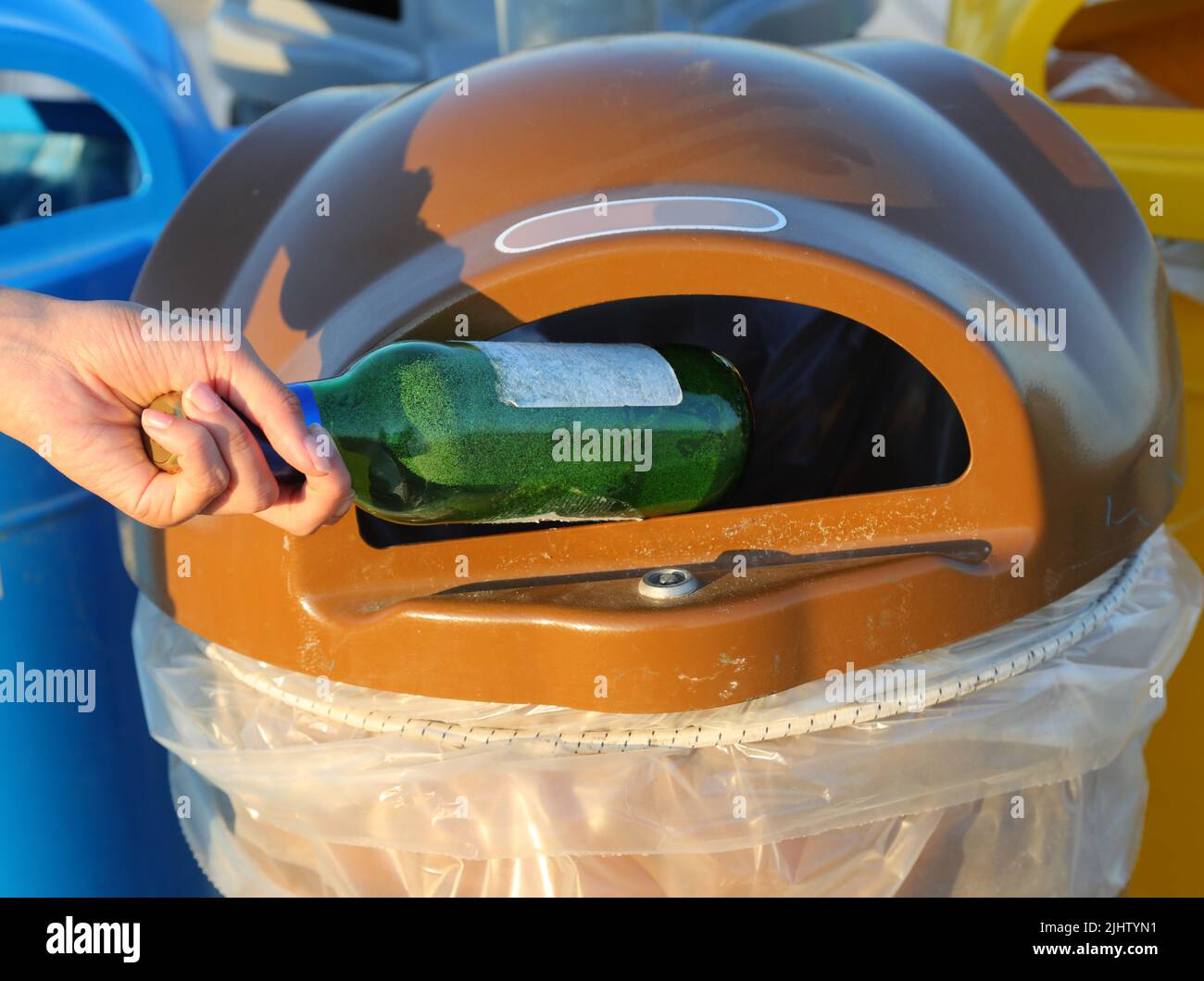hand of person throwing away a used glass bottle in the recycling bin ...