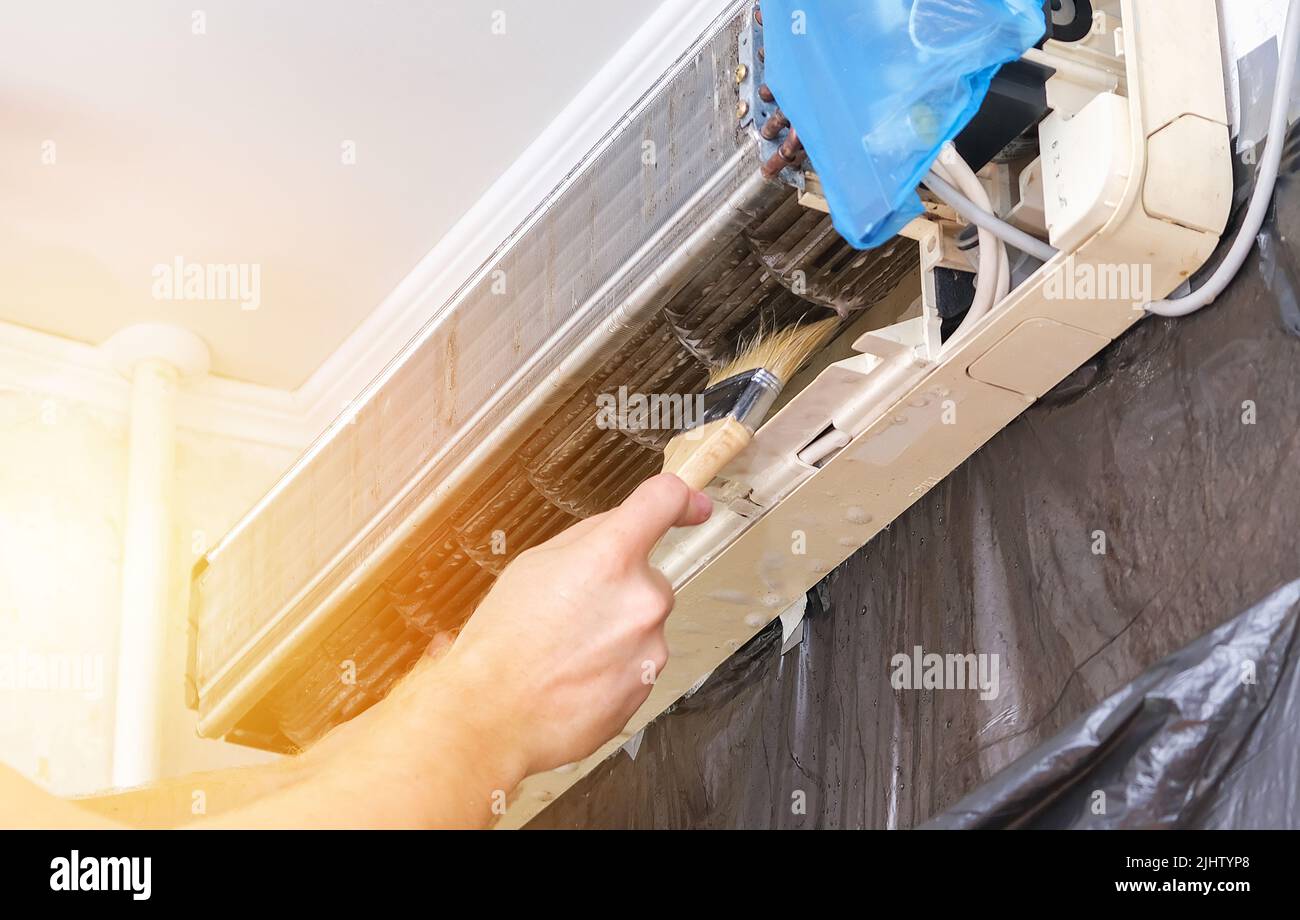 A man washes off a special foam for cleaning air conditioners with a ...