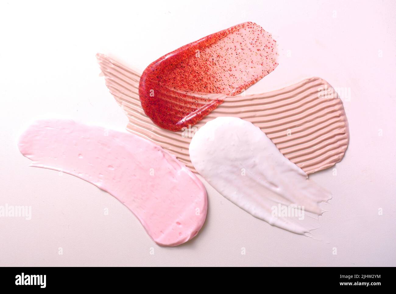 A Creamy drops of four different types of cream on pink background ...