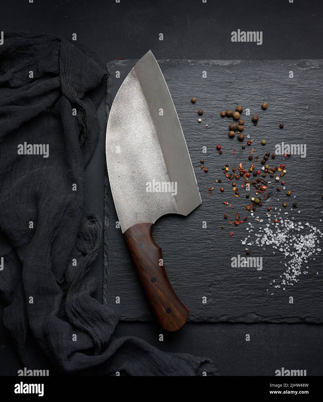 Large kitchen knife on a black graphite board and spices, top view ...