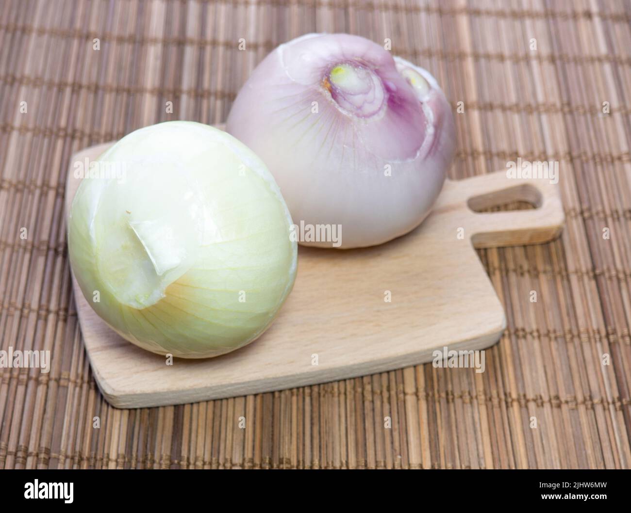 Two peeled onions on a small cutting board. Root crop before cooking ...