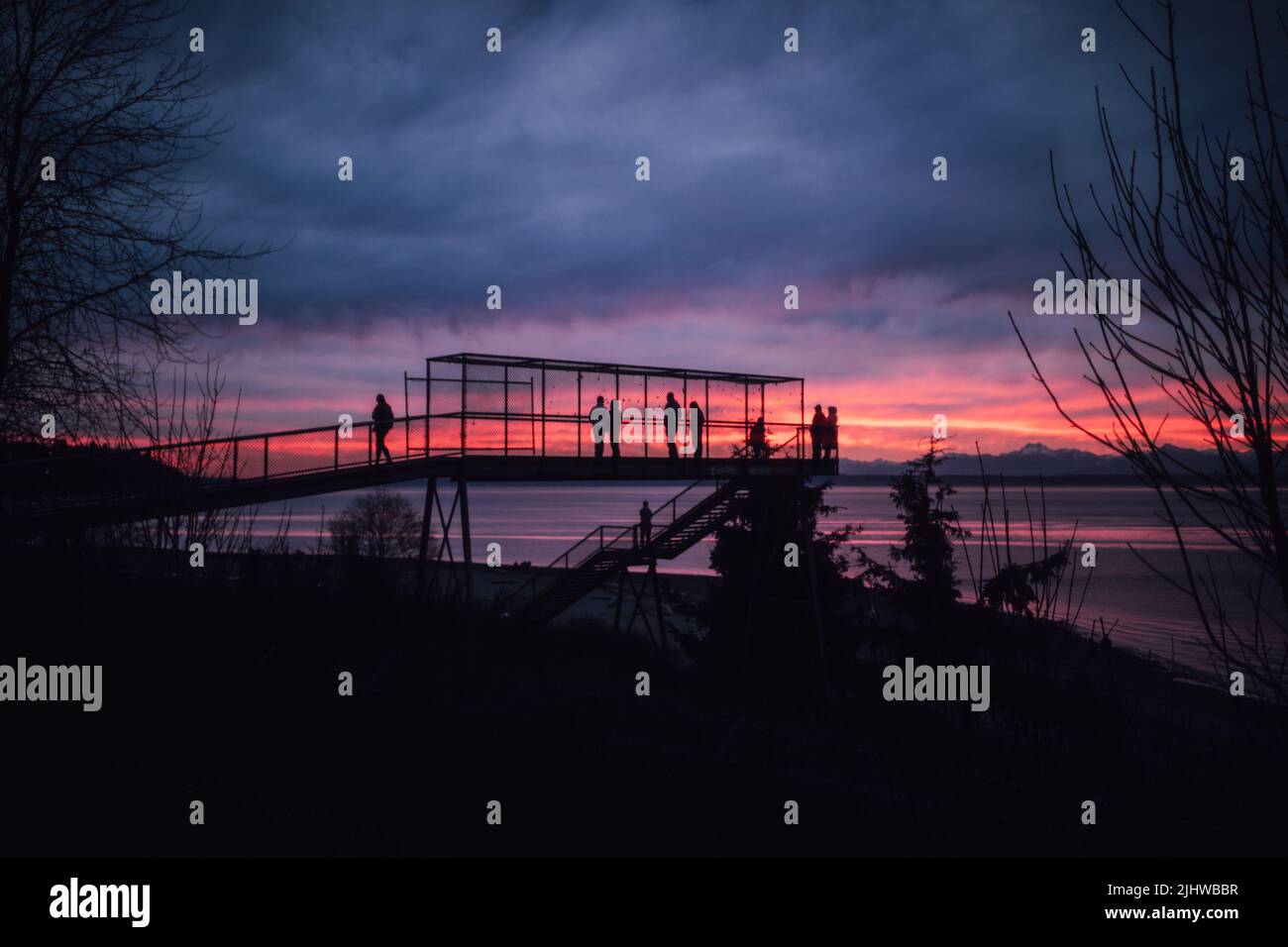 intense pink, purple, blue sunset with people on bridge over railway ...