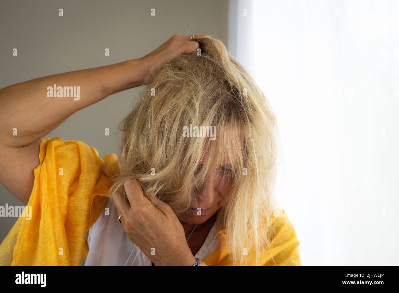 Blond woman in her 50s ruffling her hair. Concept of mental illness or ...