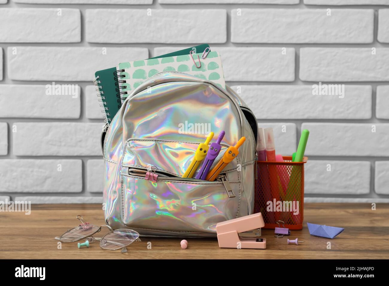 School backpack with stationery on table against white brick background ...