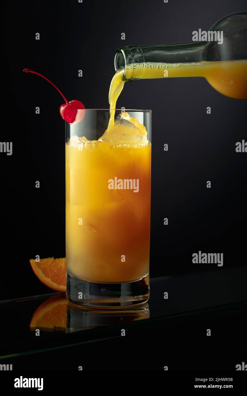 Orange juice is poured into a tall glass with ice. Cocktail preparation ...