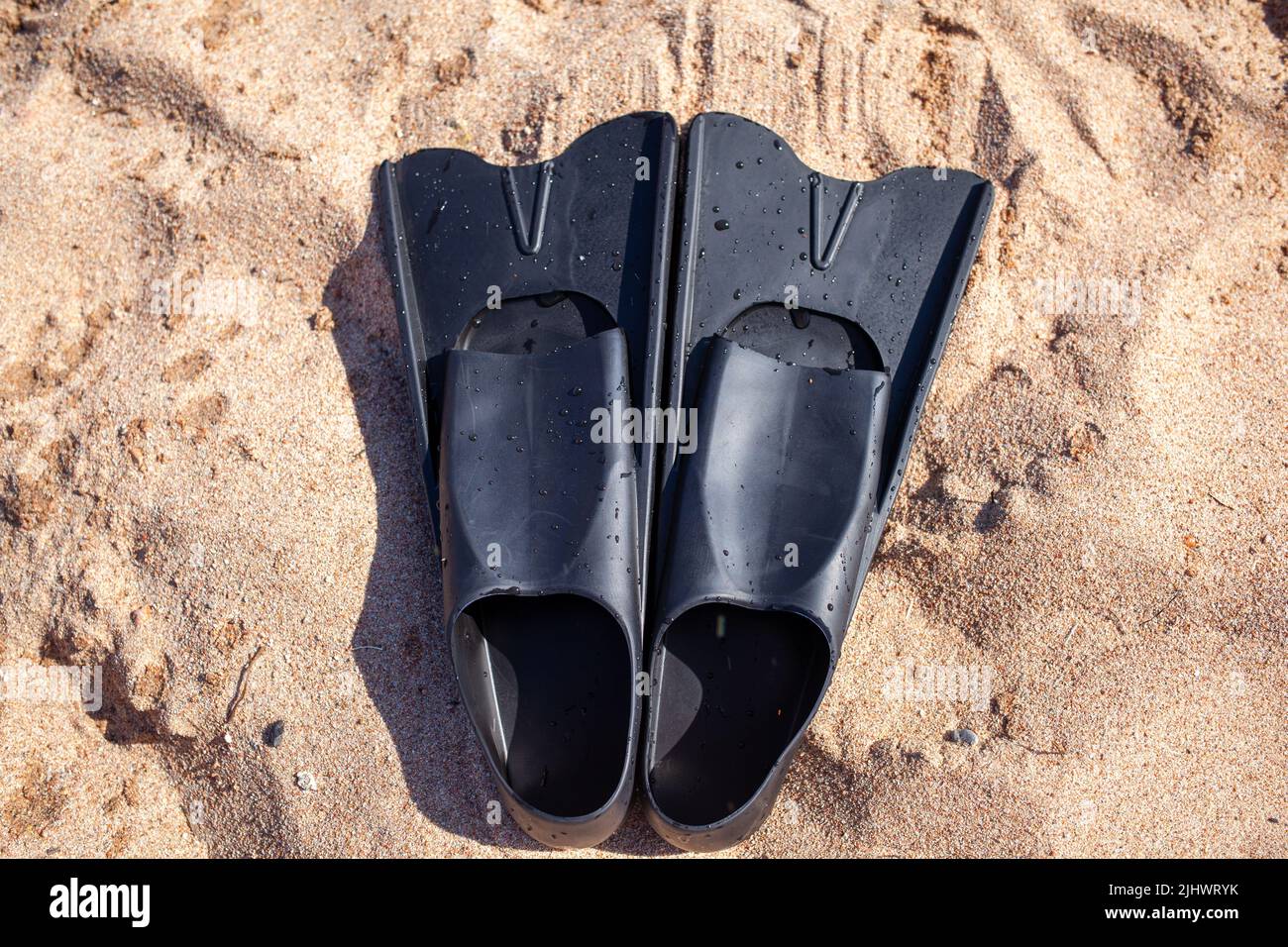A pair of black flippers on the background of sand next to the water ...
