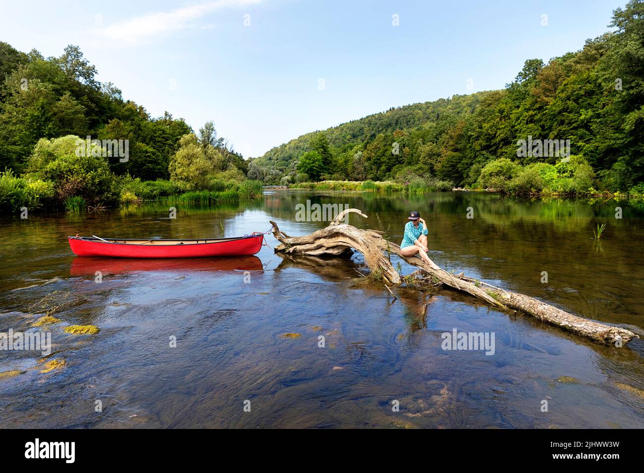 Woman Tourist sitting on a log in a river, exploring Krka river and the wilderness of its ...