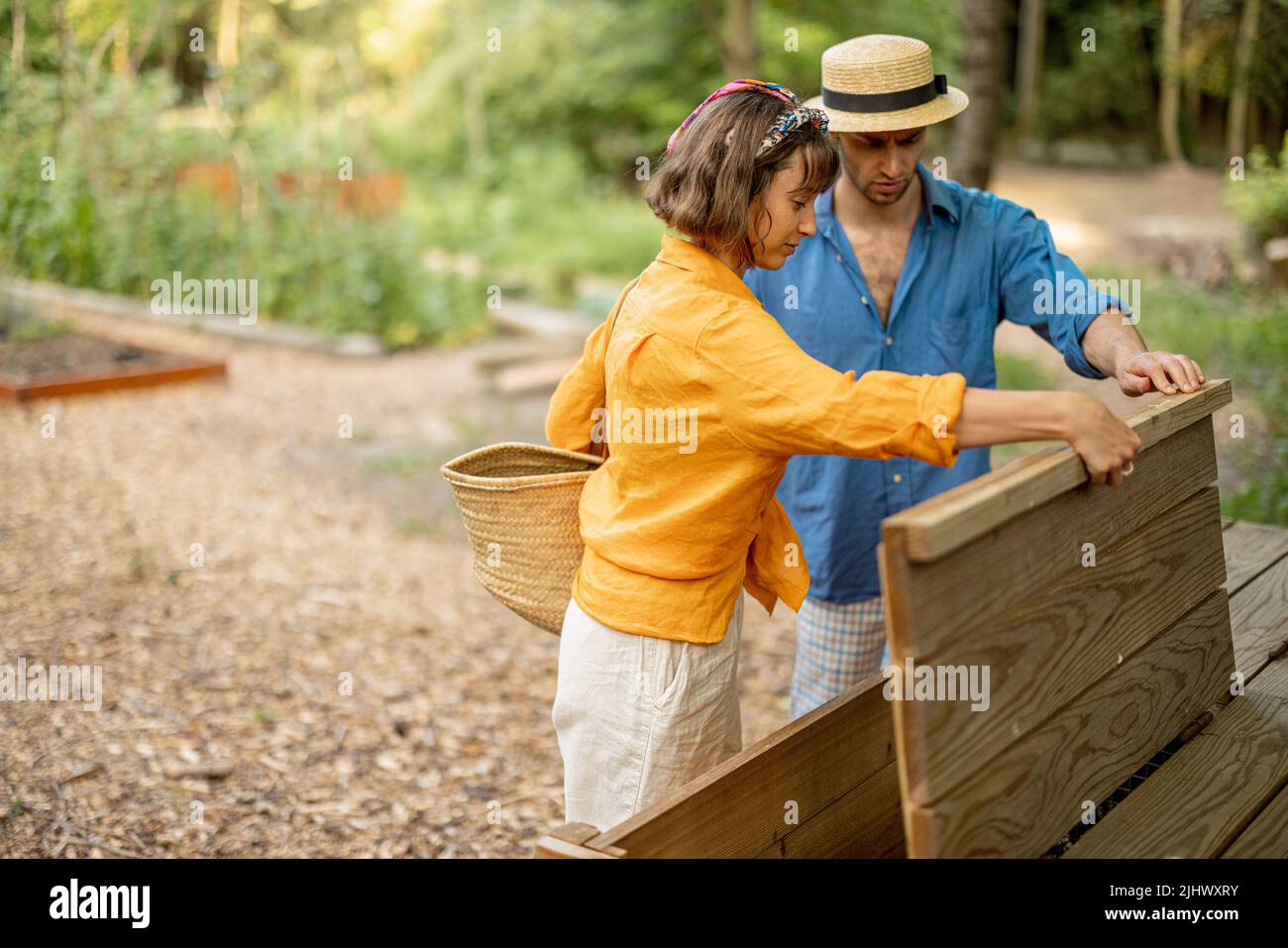Young couple throwing cut grass to compost wooden bin for rotting into ...