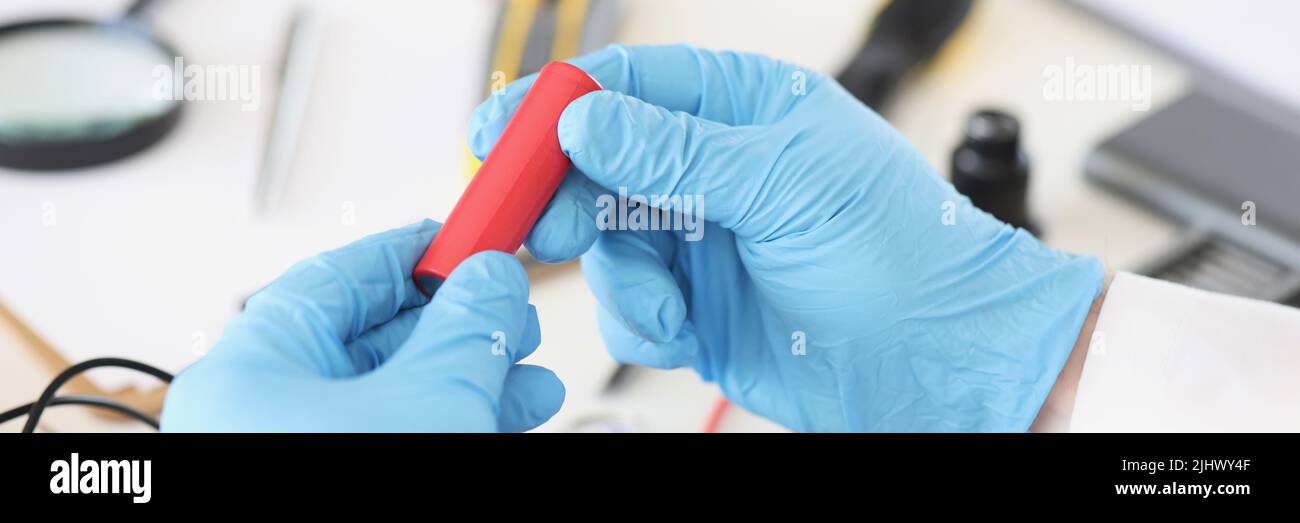 Male in blue gloves holding red battery piece, repairing broken or ...