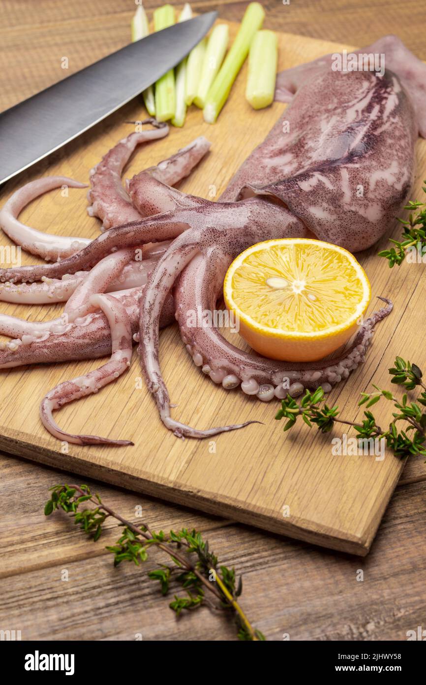 Raw squid with tentacles, lemon and knife on cutting board. Top view ...