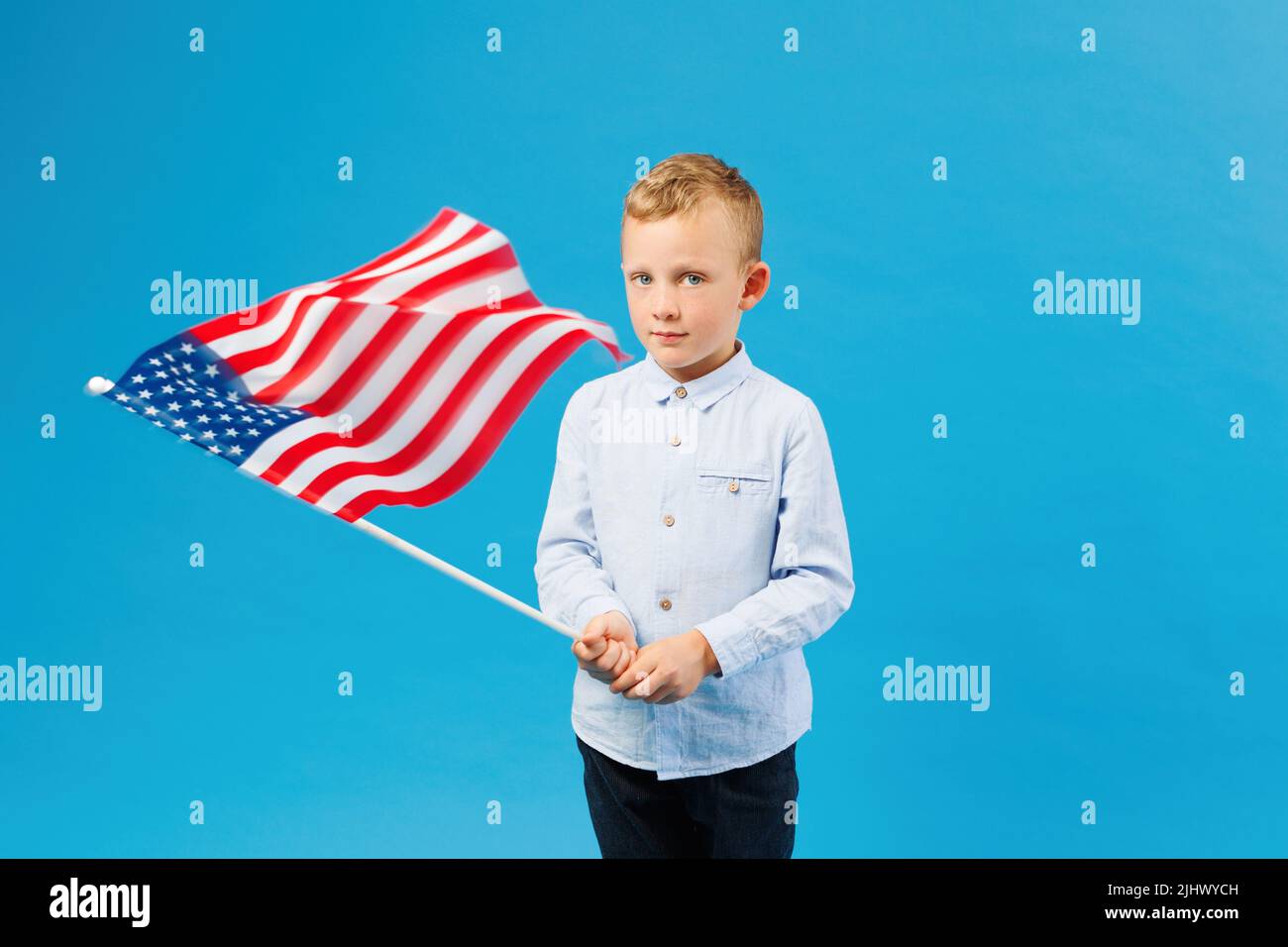 Cute boy holding American flag in indoor studio on blue background. The ...
