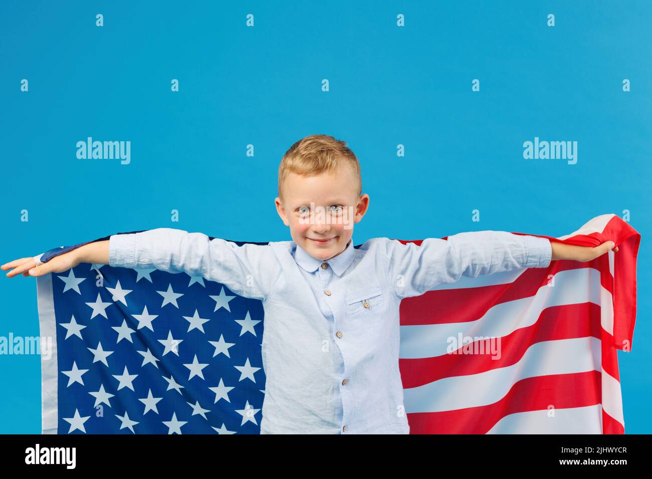 Cute boy holding American flag in indoor studio on blue background. The ...
