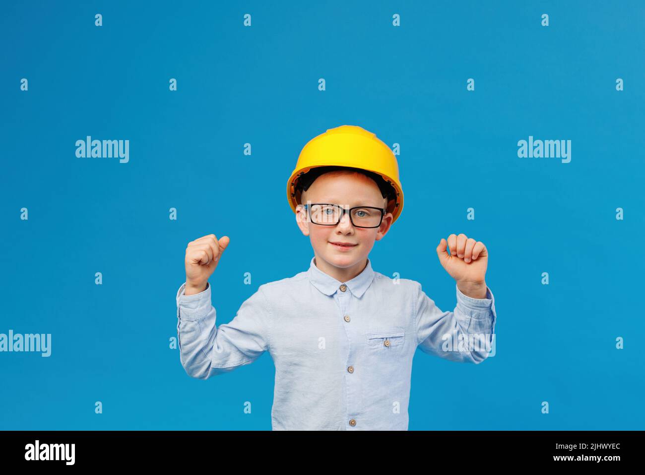 Cute boy construction worker in a yellow hard hat stands in an indoor ...