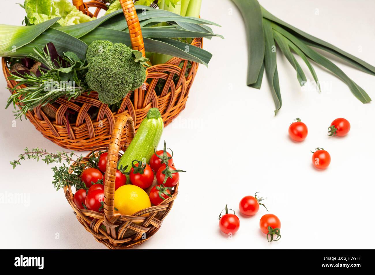 Two wicker baskets with vegetables and greens. Top view. White ...