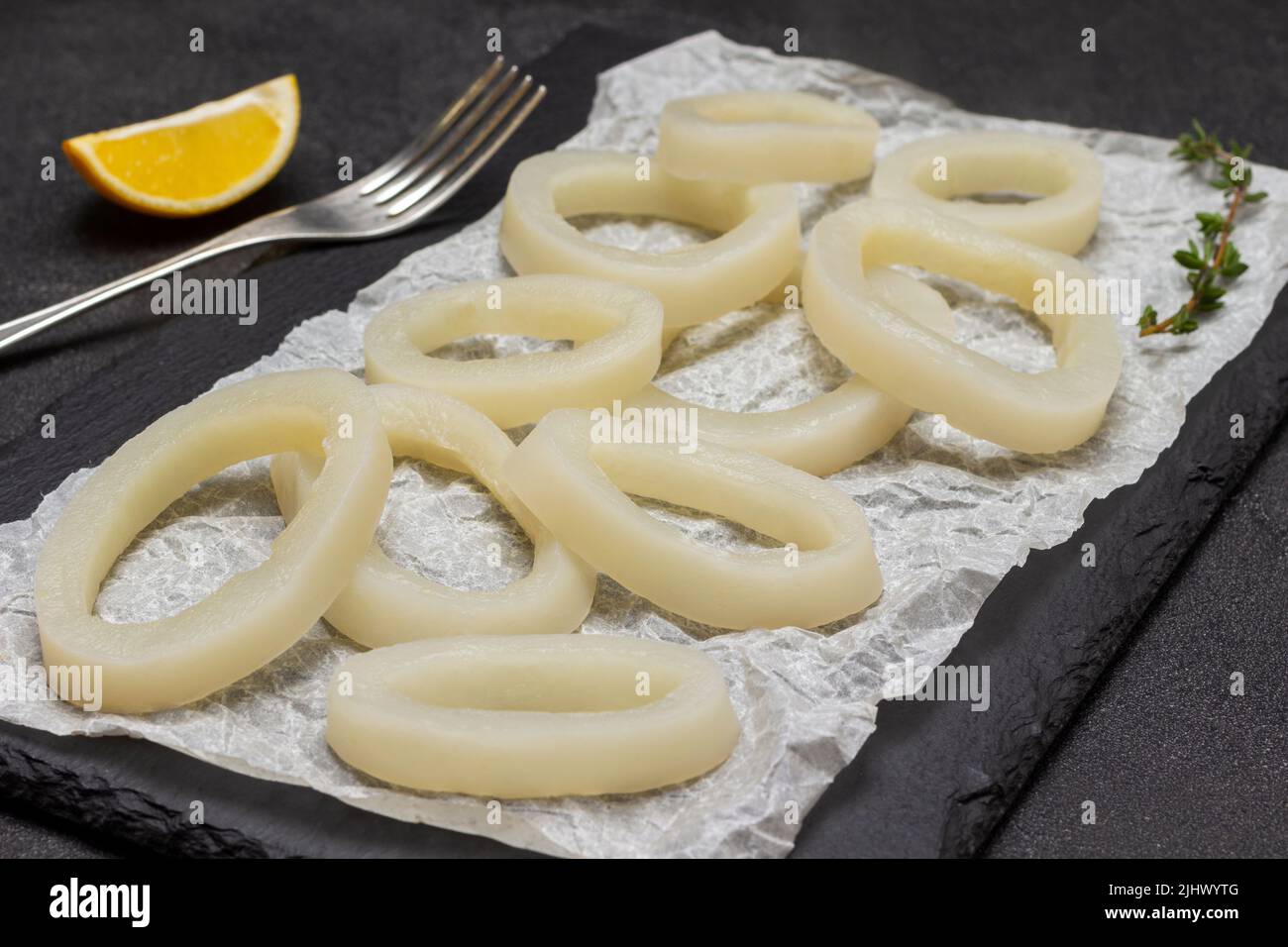 Squid cut into rings on stone board. Fork and lemon on table. Top view ...