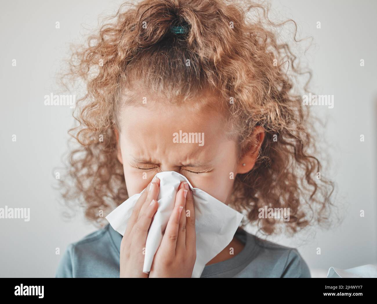 In bed is where I belong. a little sick girl blowing her nose at home ...