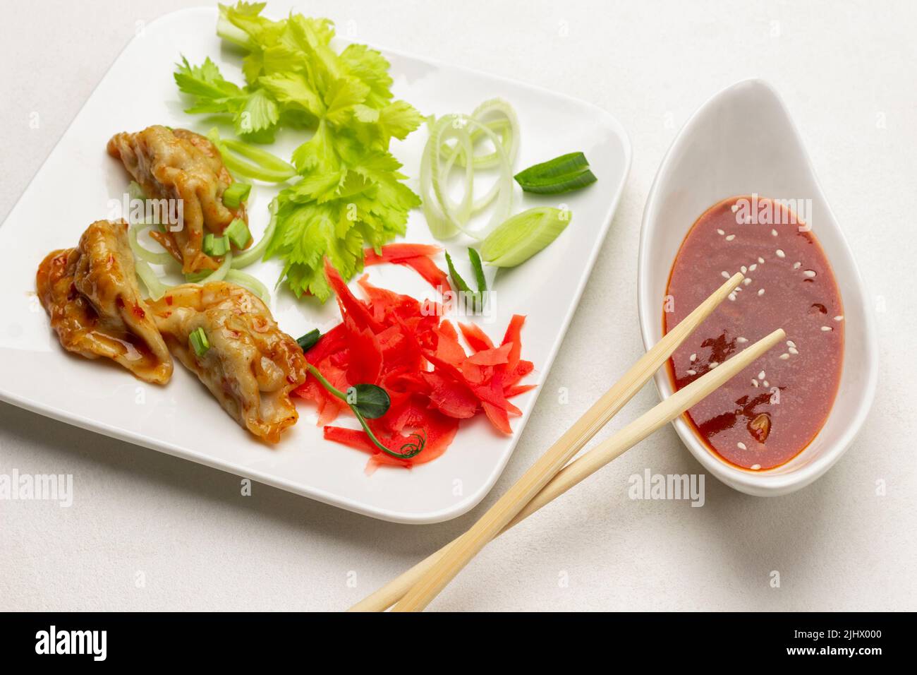 Pickled ginger, leek and gyoza dumplings and chopsticks on white plate ...
