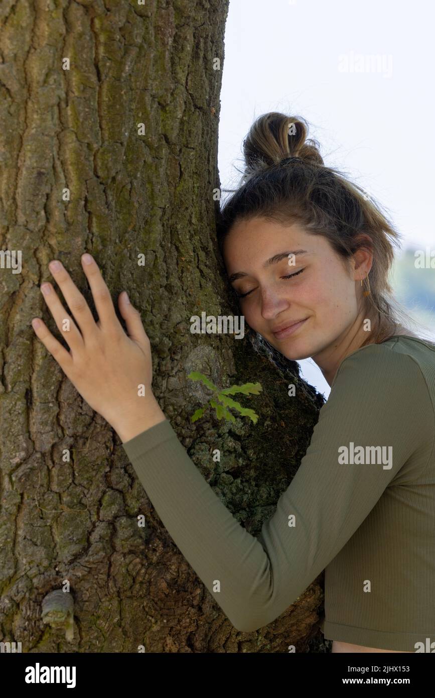 Contented young woman hugging a large tree with a blissful expression ...