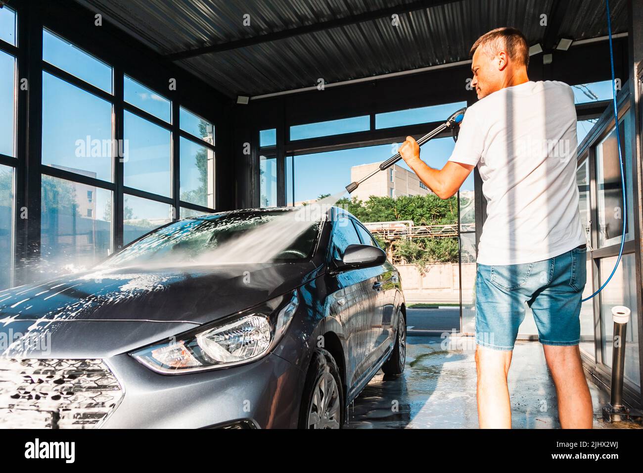 Self-service car wash. A man washes off the foam from his car with ...