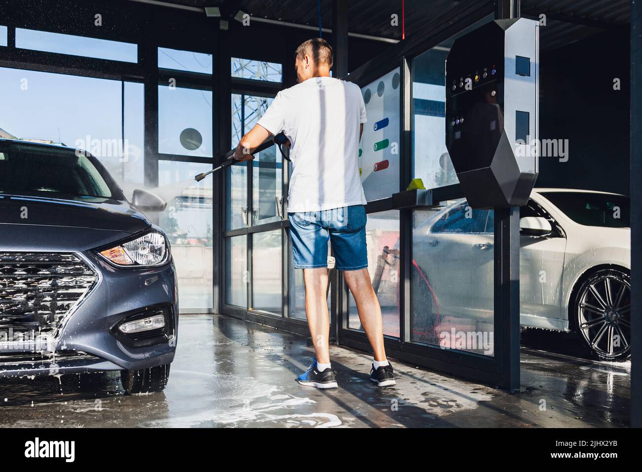 Self-service car wash. A man washes off the foam from his car with ...