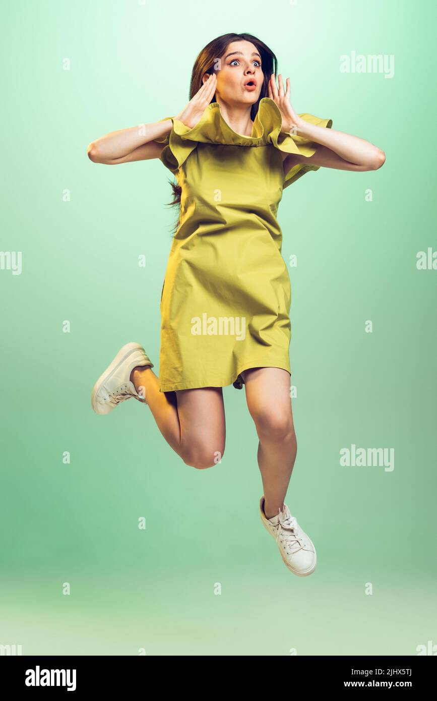 Portrait of young girl in stylish dress posing in a jump isolated over ...