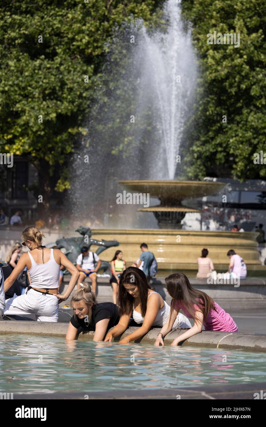 People sit cooling off with their legs in the fountains at Trafalgar ...