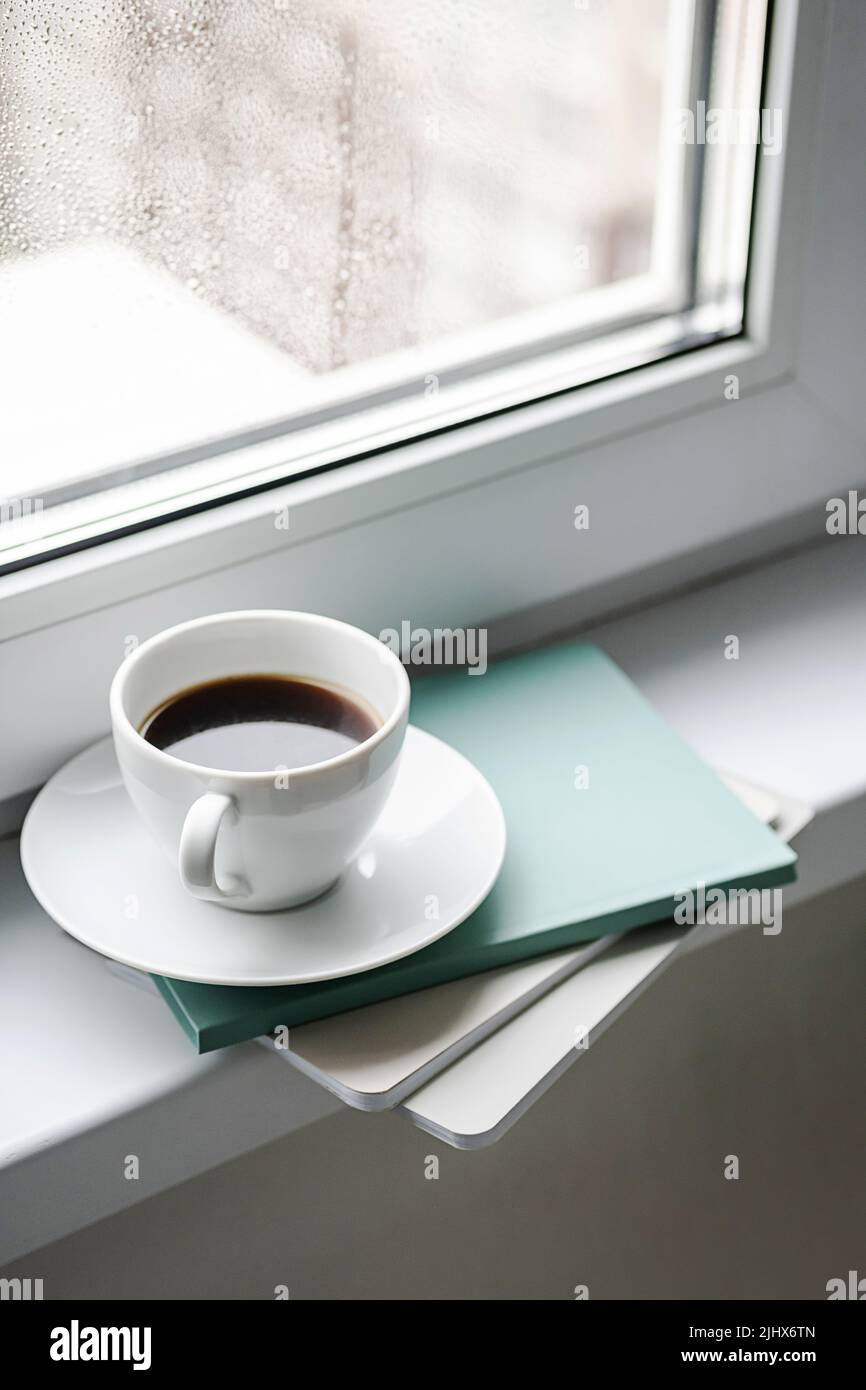 Coffee cup and books on windowsill. Cozy minimal still life against wet ...