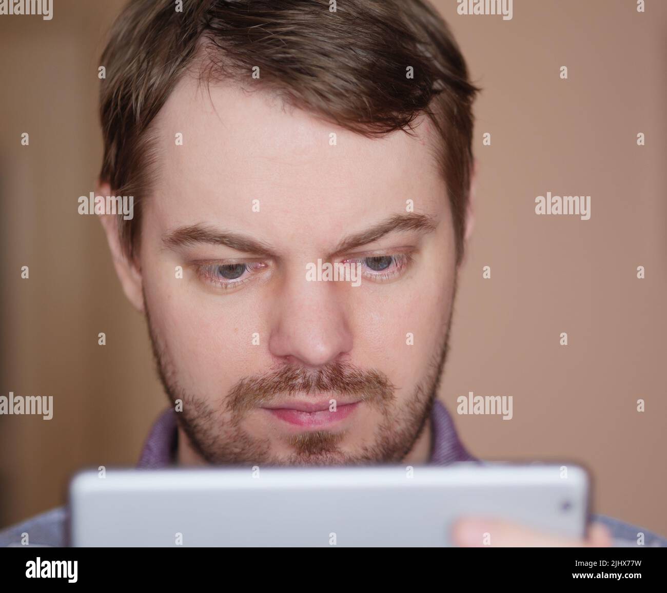Young emotional man, looking down at pda on beige background Stock ...