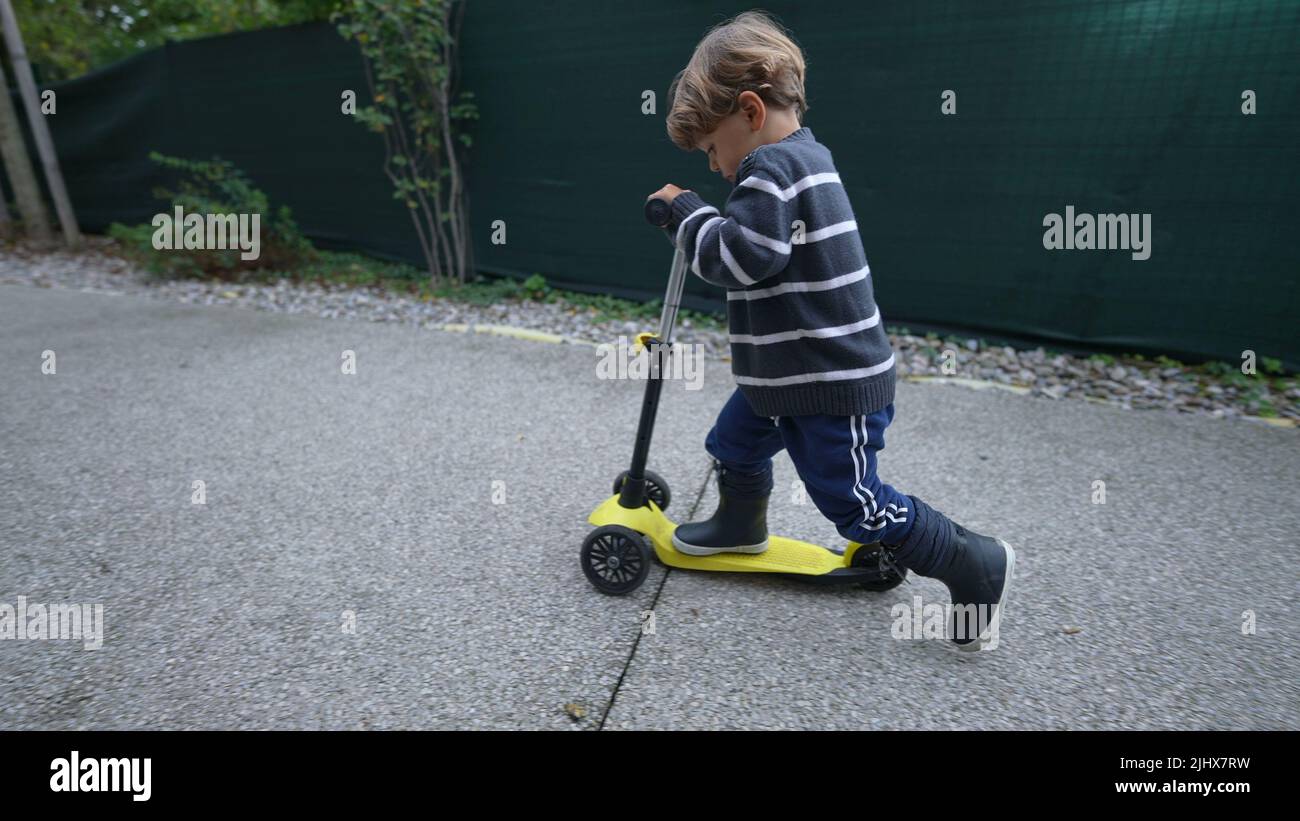 Healthy child rides three wheeled scooter, kid pushing scooter Stock ...