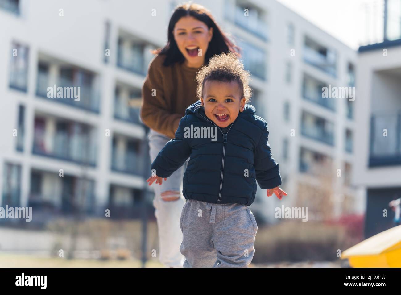 Young, grinning, Caucasian mother chasing her interracial toddler ...