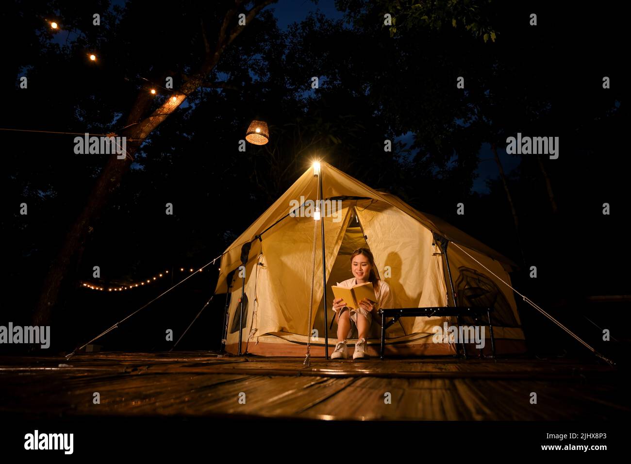 Pretty and relaxed young Asian female camper sitting in front of her ...