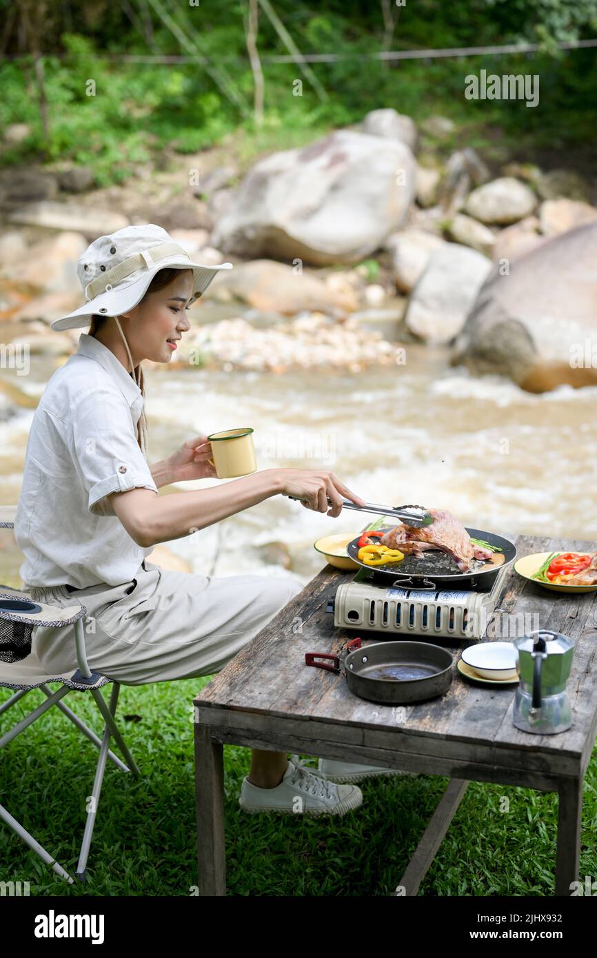 Beautiful young Asian female making a barbecue lunch for the camping ...