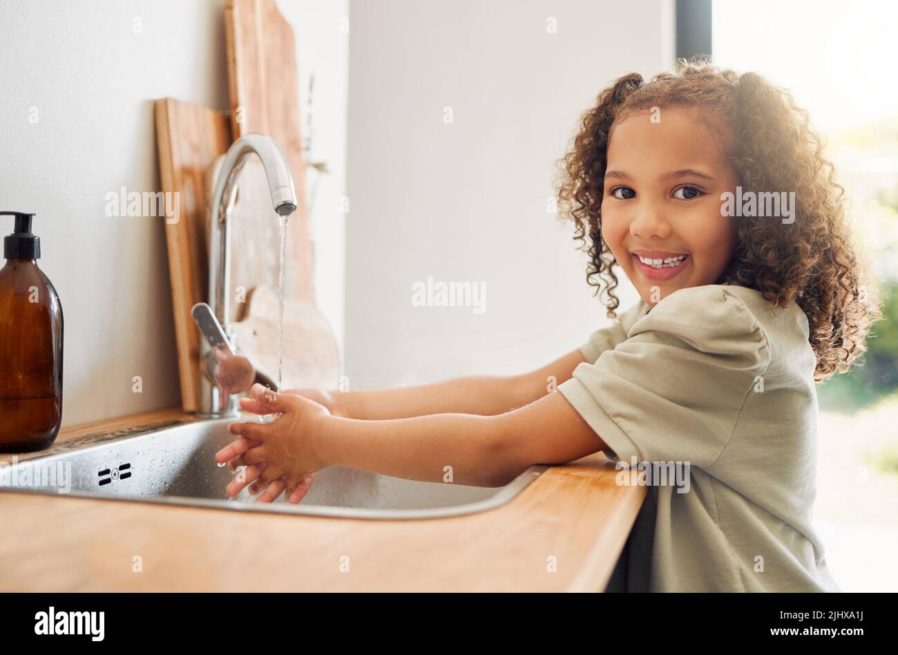 One mixed race adorable little girl washing her hands in a kitchen sink ...