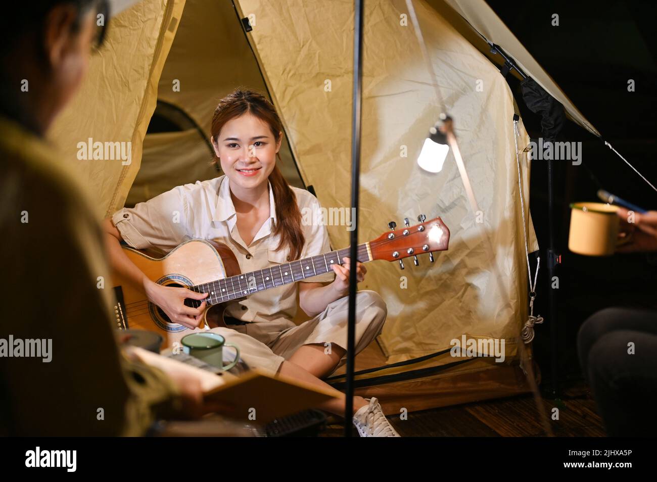 Beautiful millennial Asian female playing guitar while enjoy camping ...