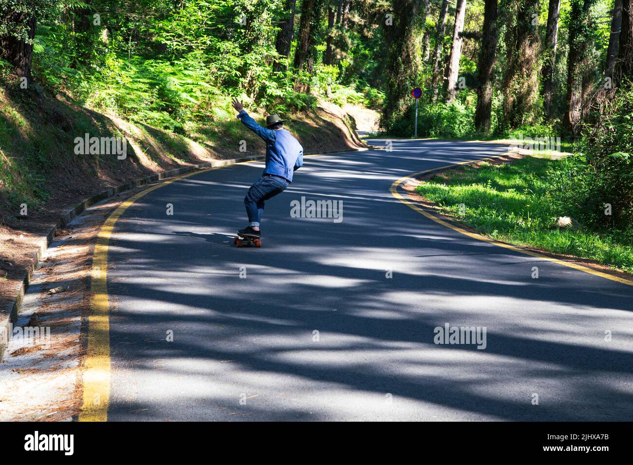 Man riding a longboard on a road through the woods Stock Photo - Alamy
