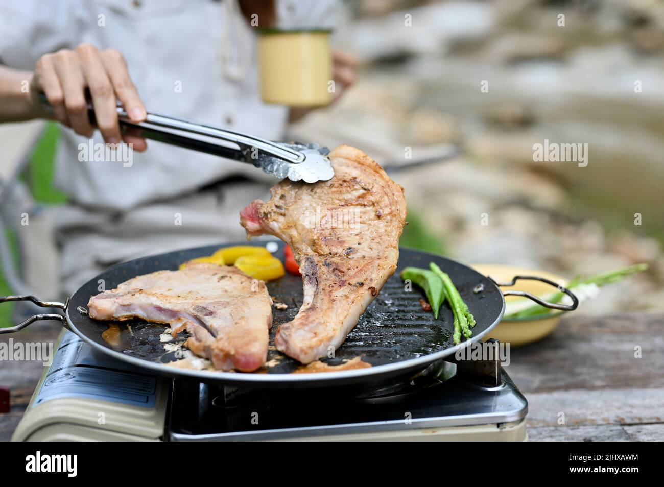 Female roasting a pork chop beef steak on a flying pan, cooking with a ...