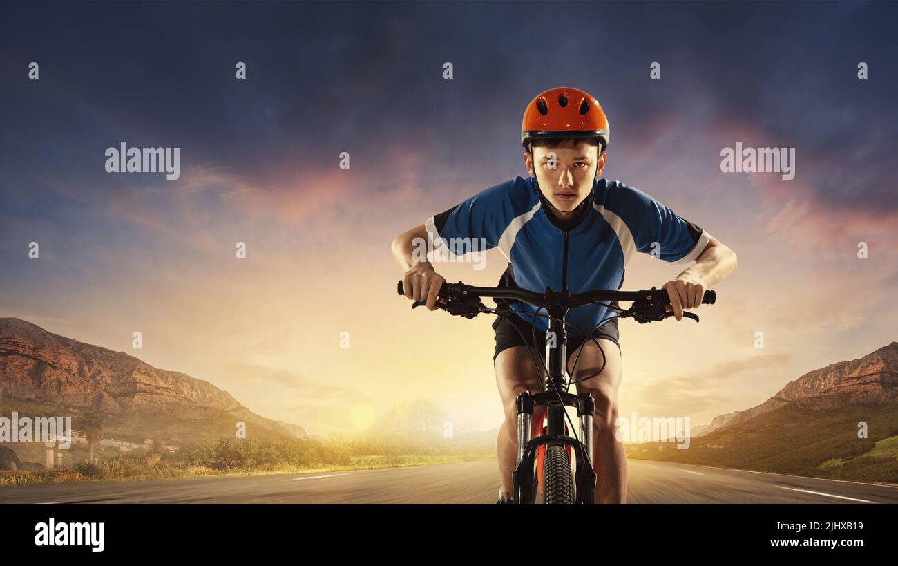 Portrait of young boy in helmet and uniform riding road on bike ...