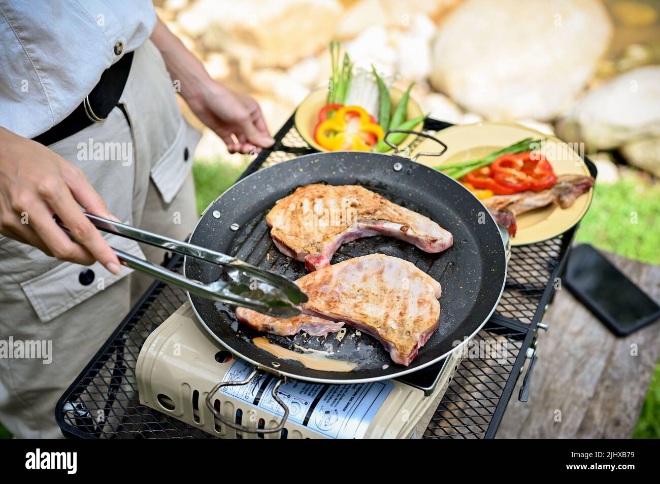 Female roasting a pork chop beef steak on a flying pan, cooking with a ...