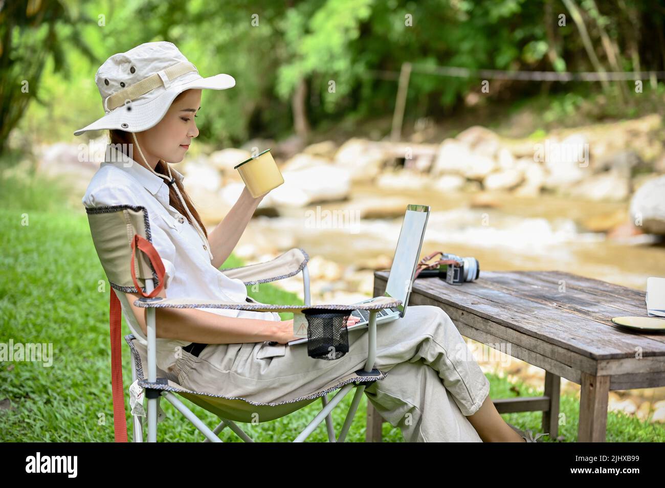 Relaxed young Asian female camper using laptop computer, sipping coffee ...