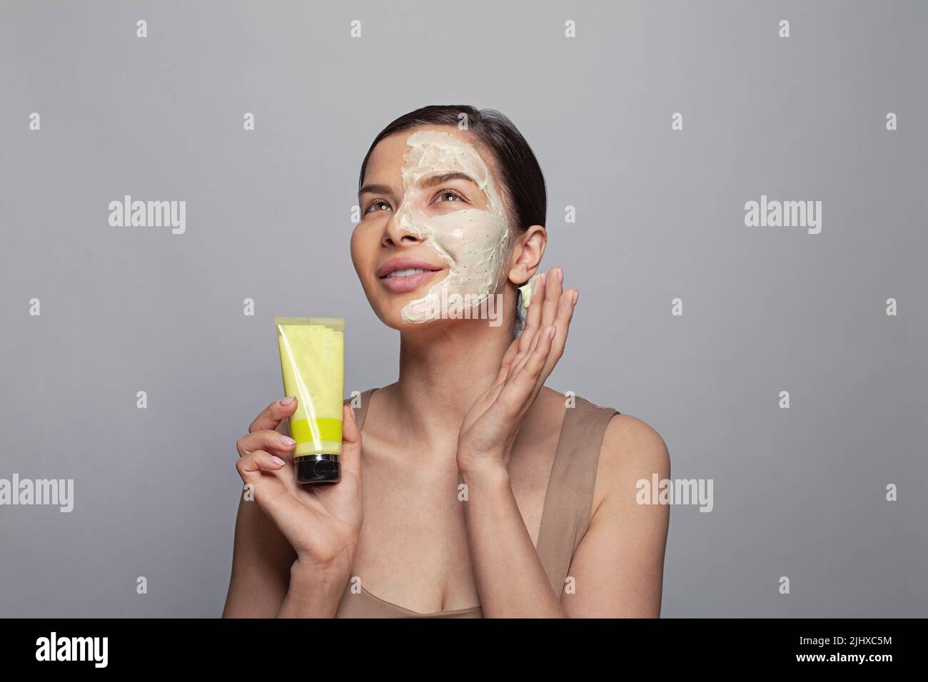 Happy spa model woman with cosmetic mask holding green cosmetic tube ...