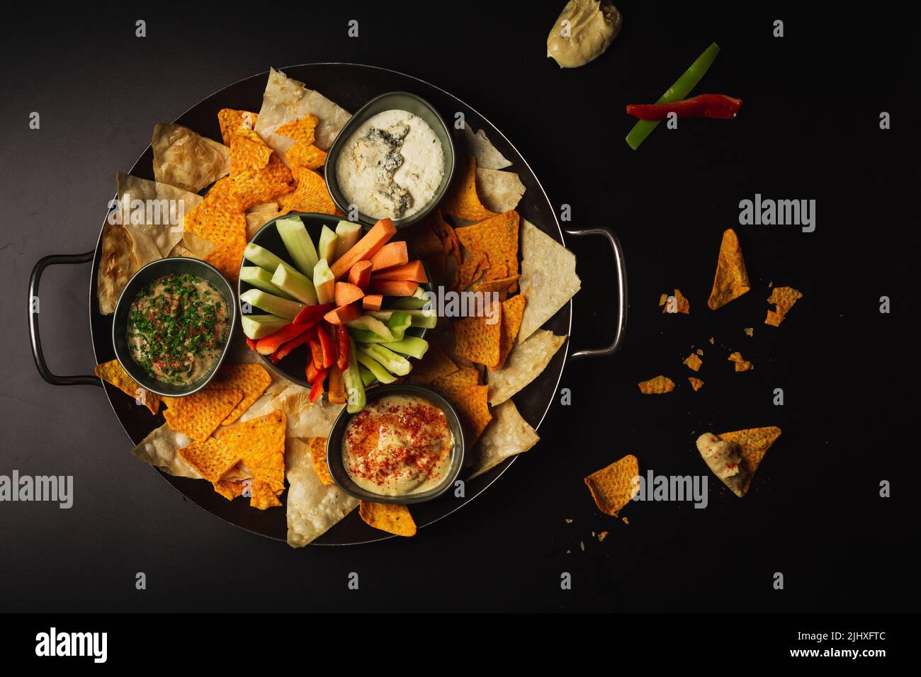A top shot of an appetizer bowl with chopped vegetable chips and souses ...