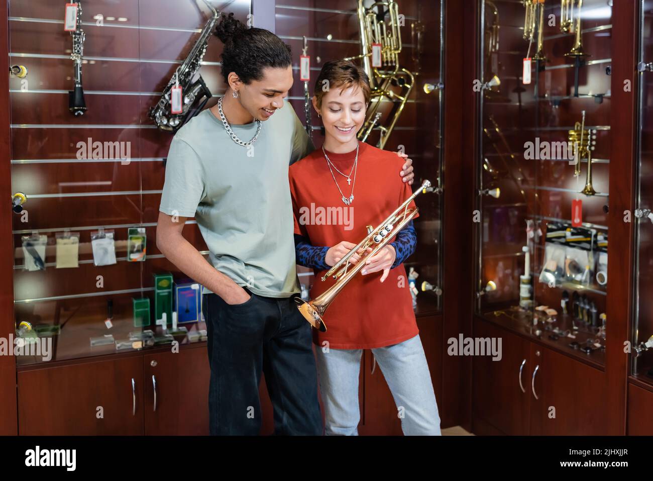 African american man hugging cheerful girlfriend with trumpet in music ...