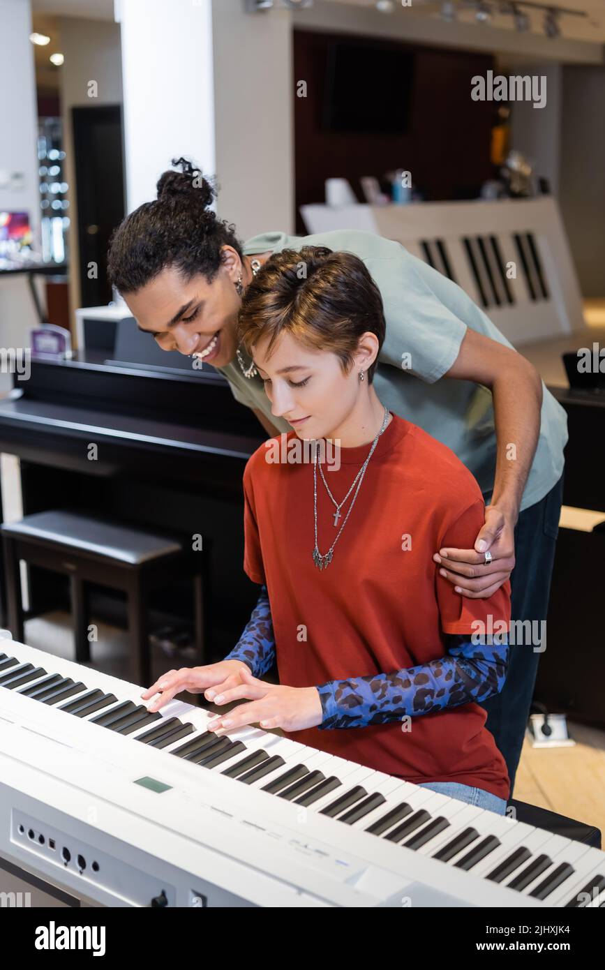 Cheerful african american man hugging girlfriend playing synthesizer in ...