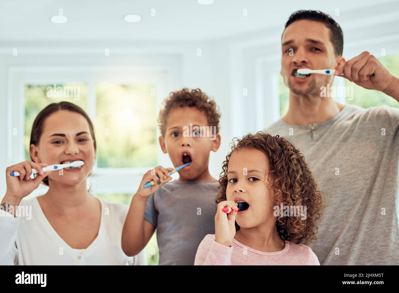 Happy mixed race parents and their two children brushing their teeth ...