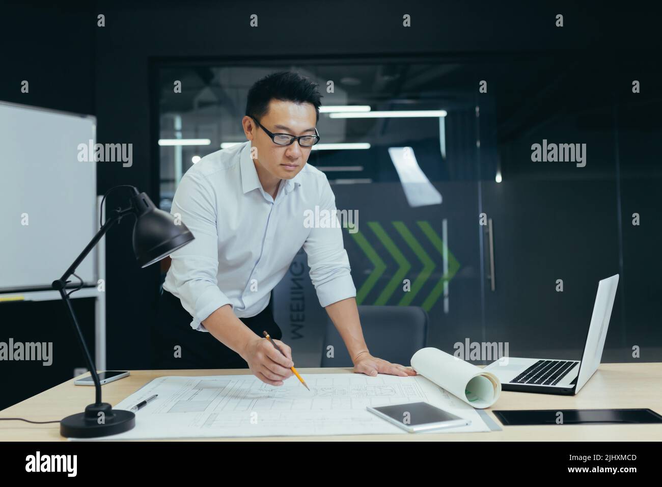 Successful Asian architect works in design studio, on plan drawing of ...