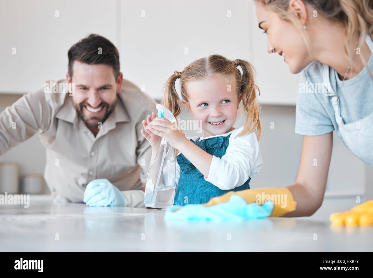 Happy family cleaning the kitchen together. Little girl spraying ...
