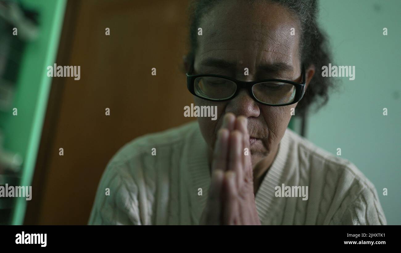 Religious older person praying at home. One hispanic senior woman prays ...