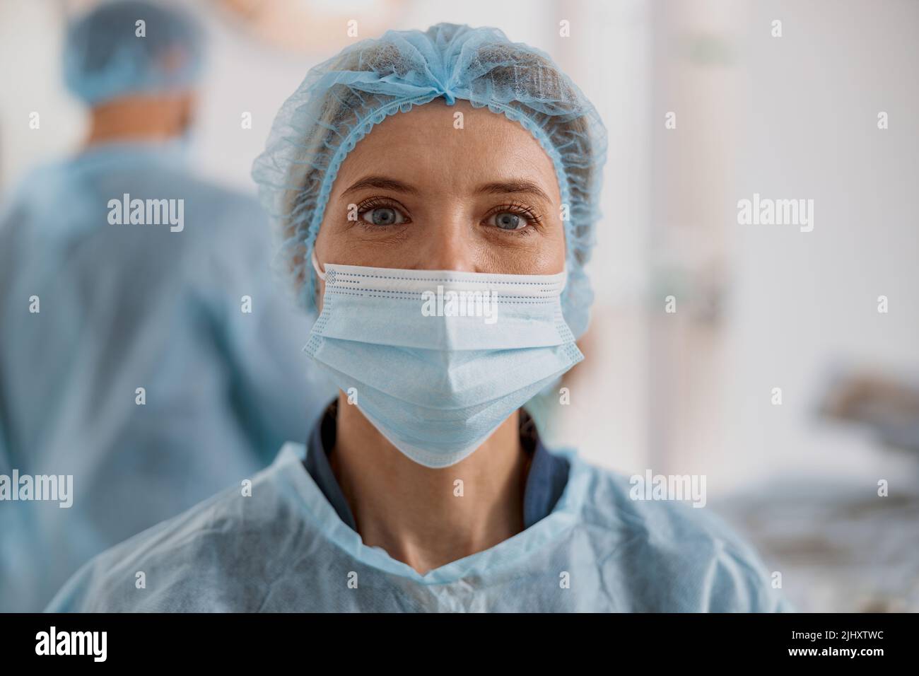 Portrait of female surgeon in mask standing in operating room, ready to ...