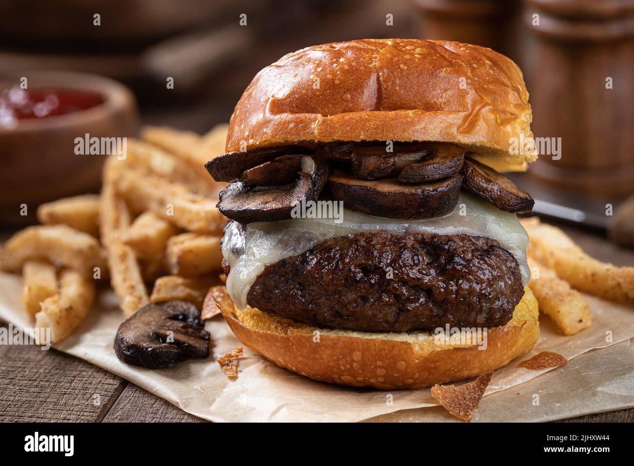 Closeup of cheeseburger with mushrooms on toasted bun with french fries ...