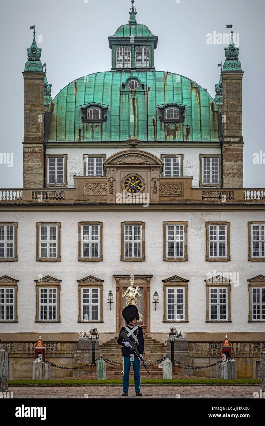 A vertical shot of the Frederiksborg Castle with a guard standing by ...